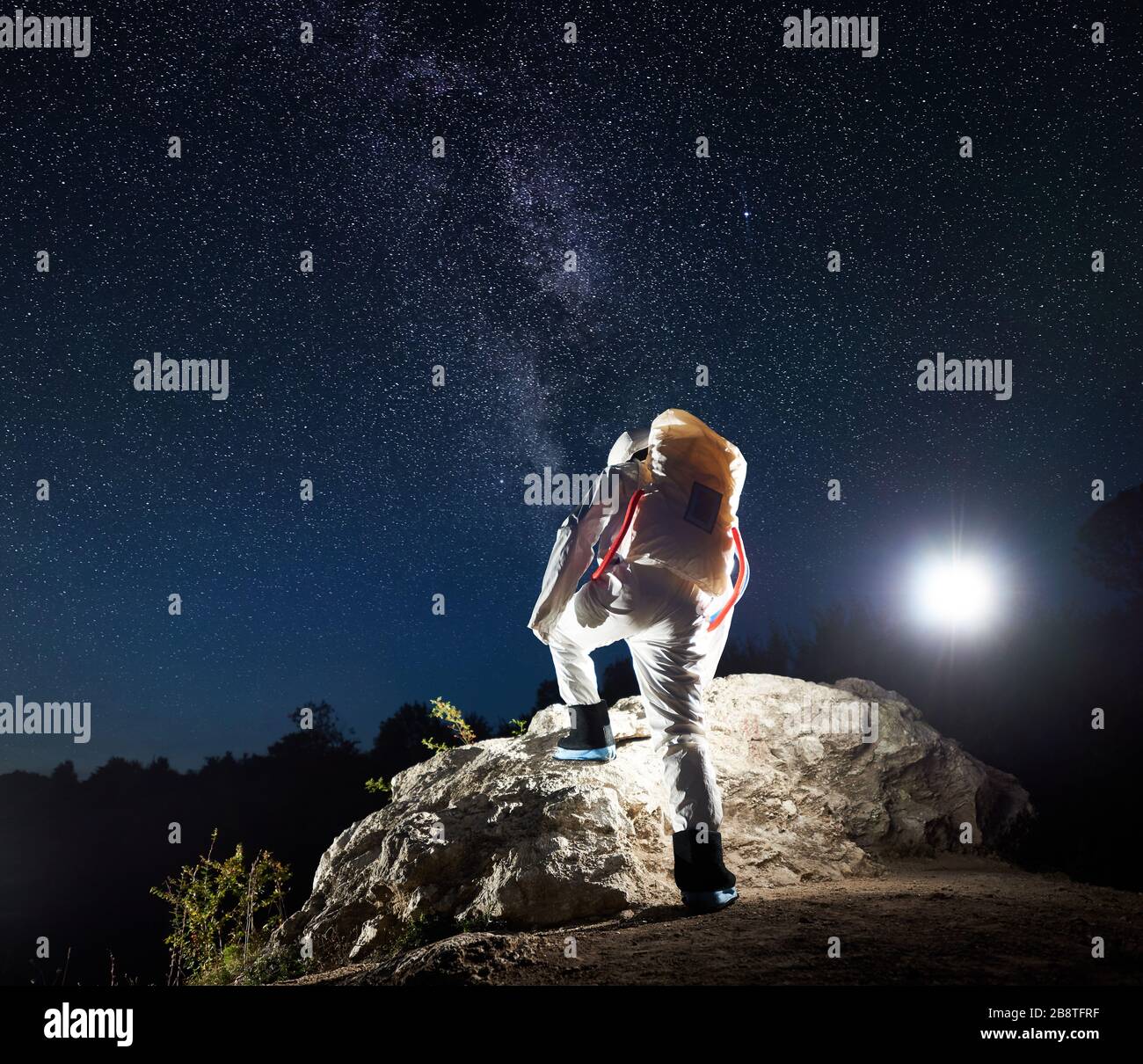 Back view of space traveler climbing up rocky cliff under beautiful ...