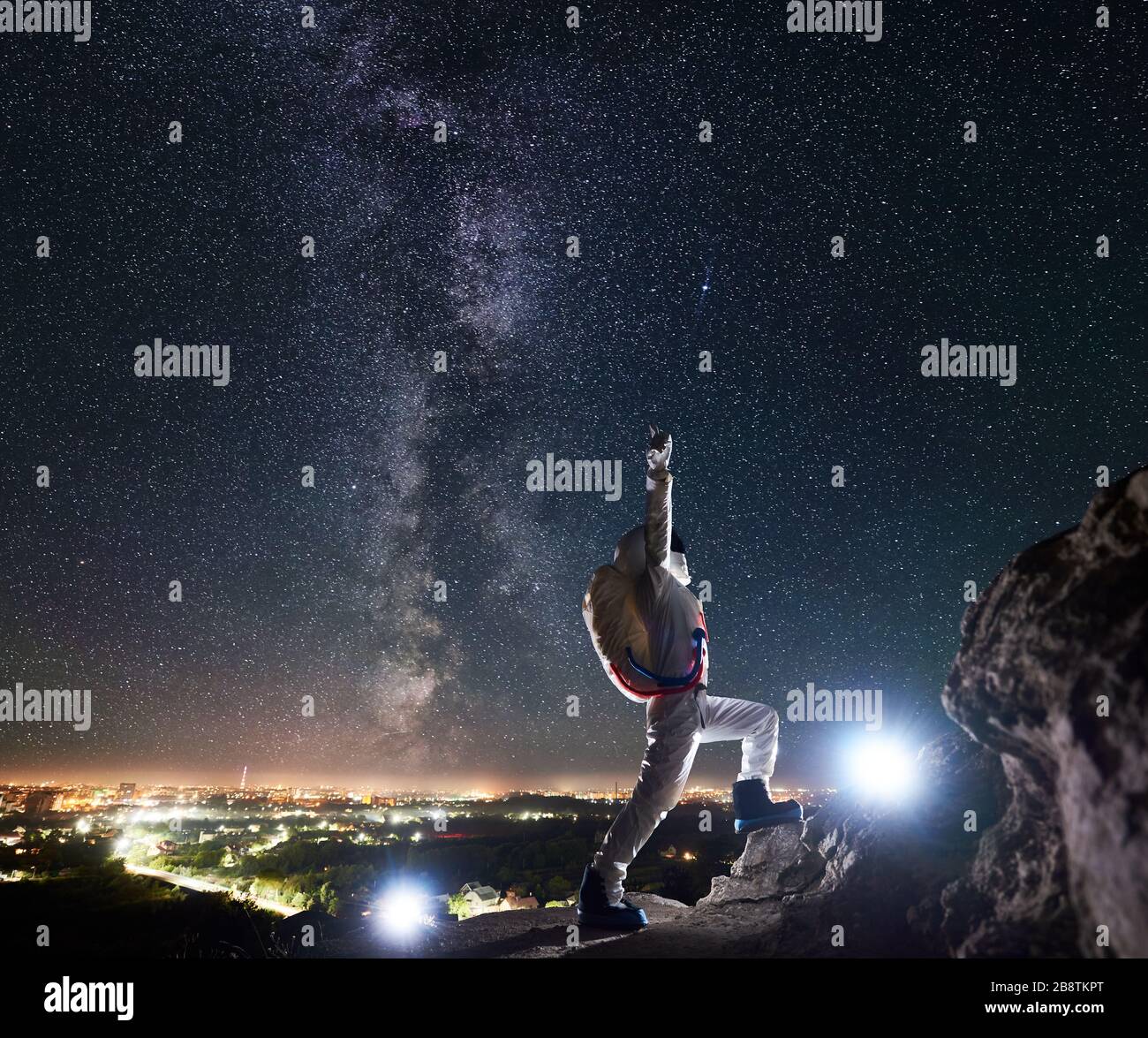 Side view of spaceman raising arms while standing on rocky hill under ...