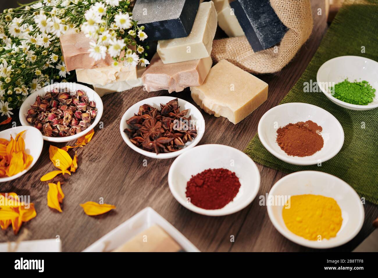 Ceramic bowls with powder colorants and dry flowers on table in soap ...