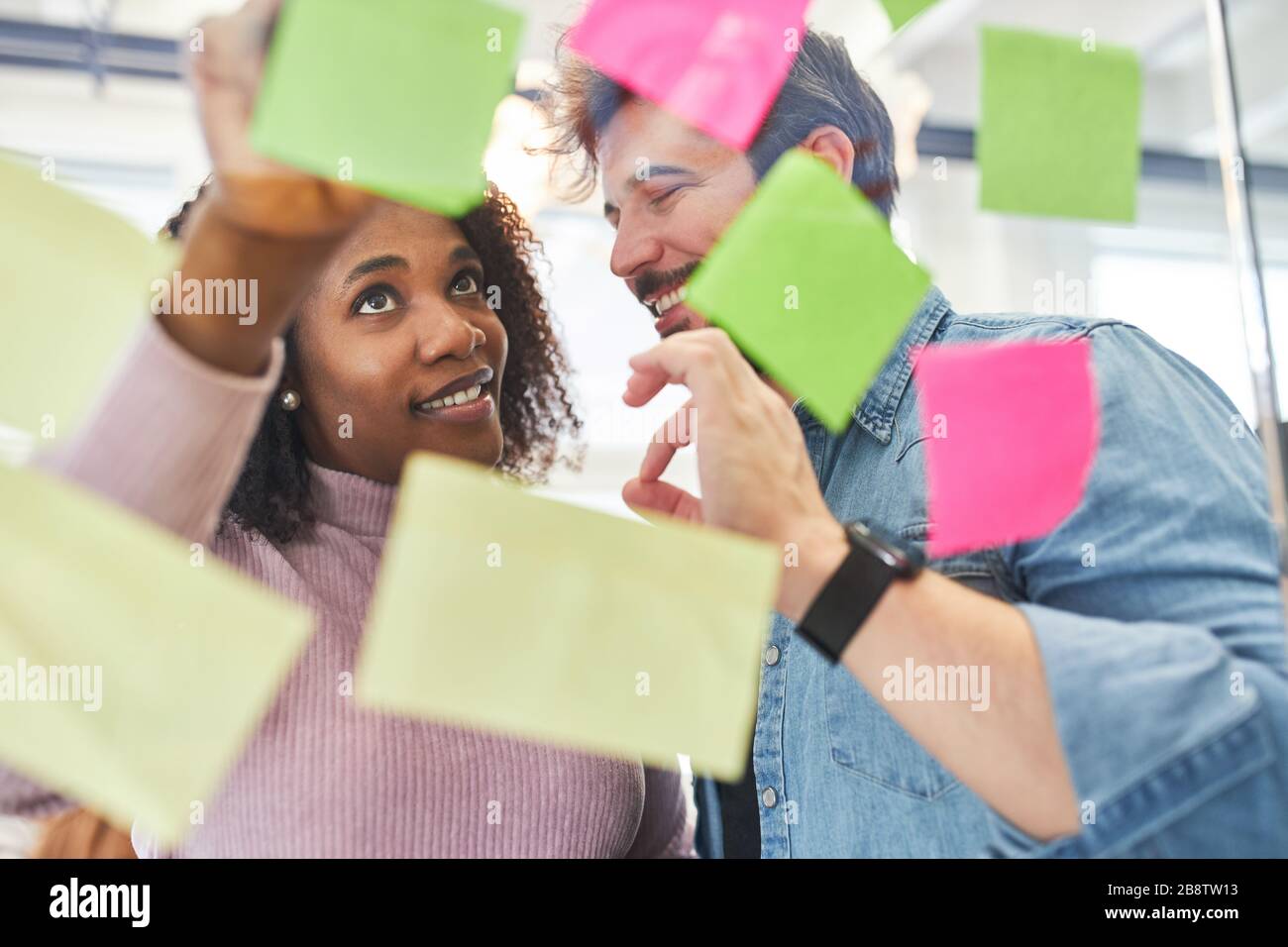Two students or trainees brainstorming with sticky notes on glass wall ...