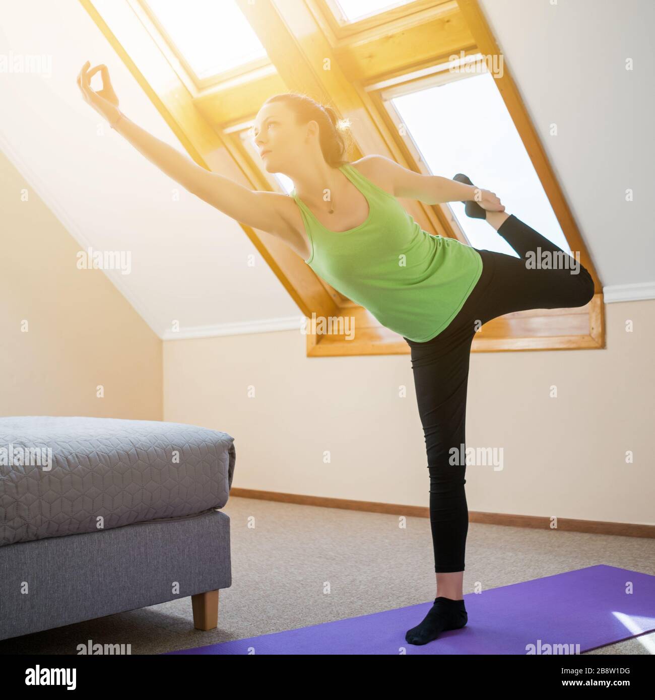 Young woman is practicing yoga at home. Natarajasana / Shiva posture ...