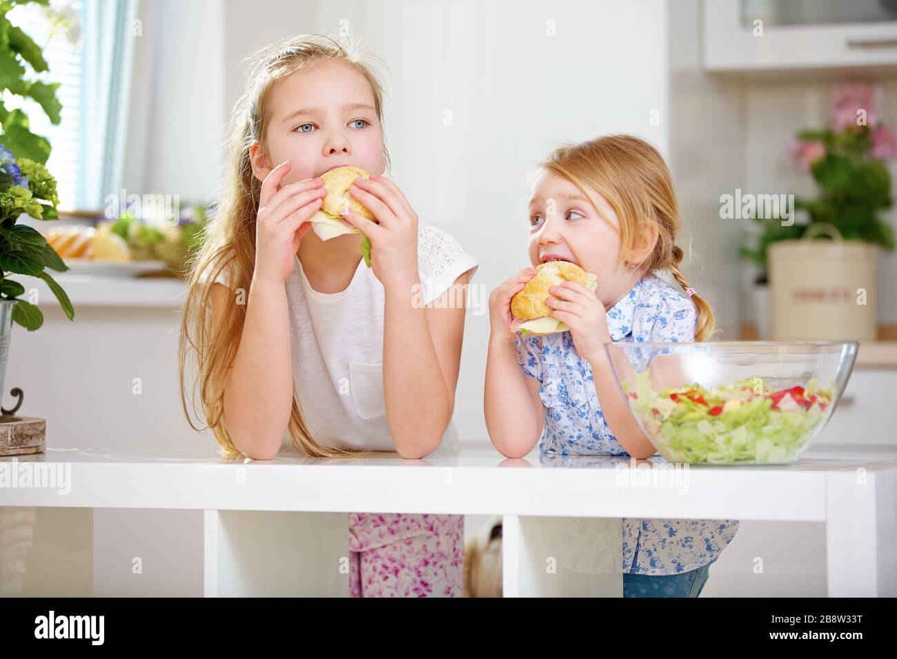 Two children of a family eat bread rolls for breakfast in the kitchen ...