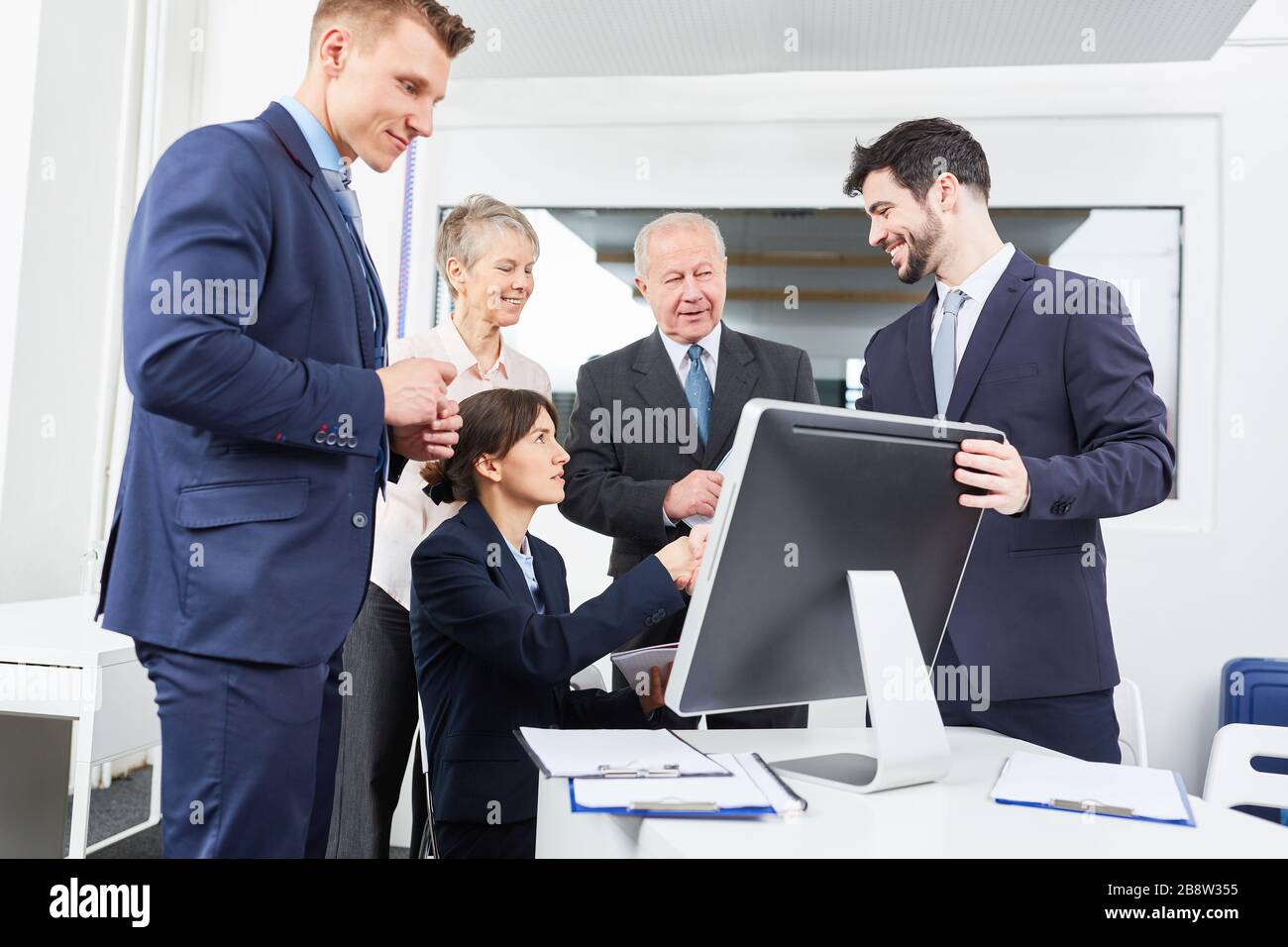 Group of business people is standing around a computer monitor in the ...
