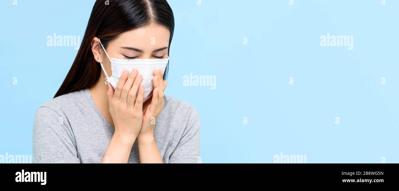 Asian woman wearing medical face mask coughing isolated on light blue ...