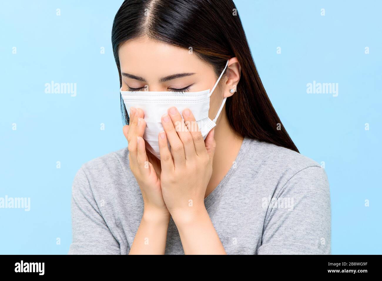 Asian woman wearing medical face mask coughing isolated on light blue ...