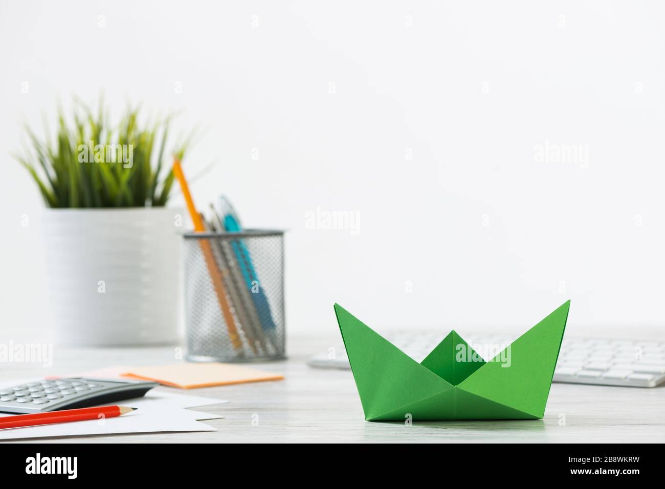 Wooden office desk with green origami boat Stock Photo - Alamy