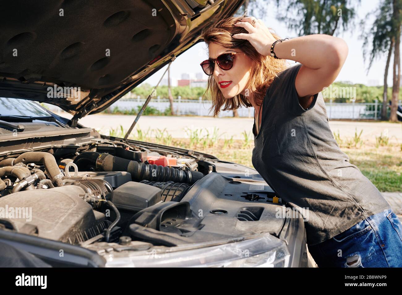 Stressed young woman opening car hood and looking at engine of broken ...