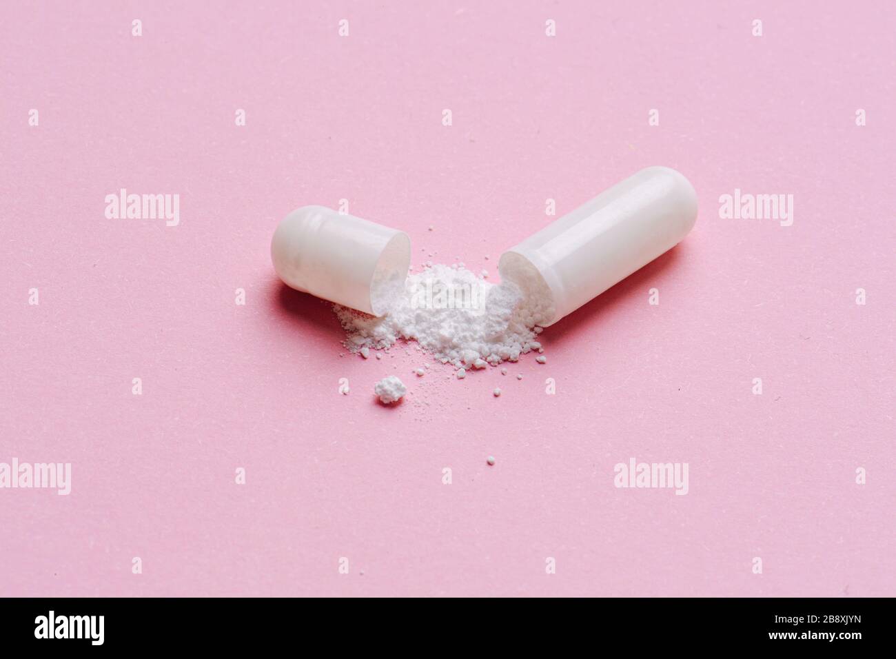 Broken white drug capsule close up on a pink surface Stock Photo - Alamy
