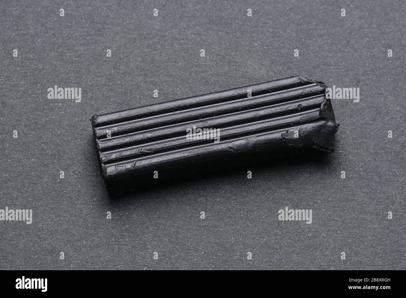 Black bar of plasticine on dark grey surface. High angle, close up ...