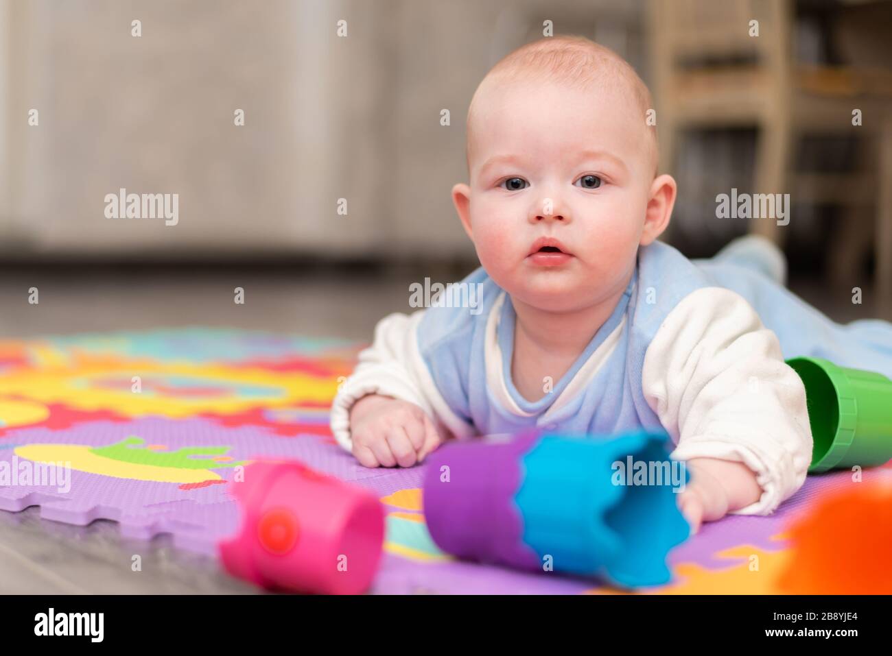 A child plays on the floor. The baby is lying on his belly on rug with ...
