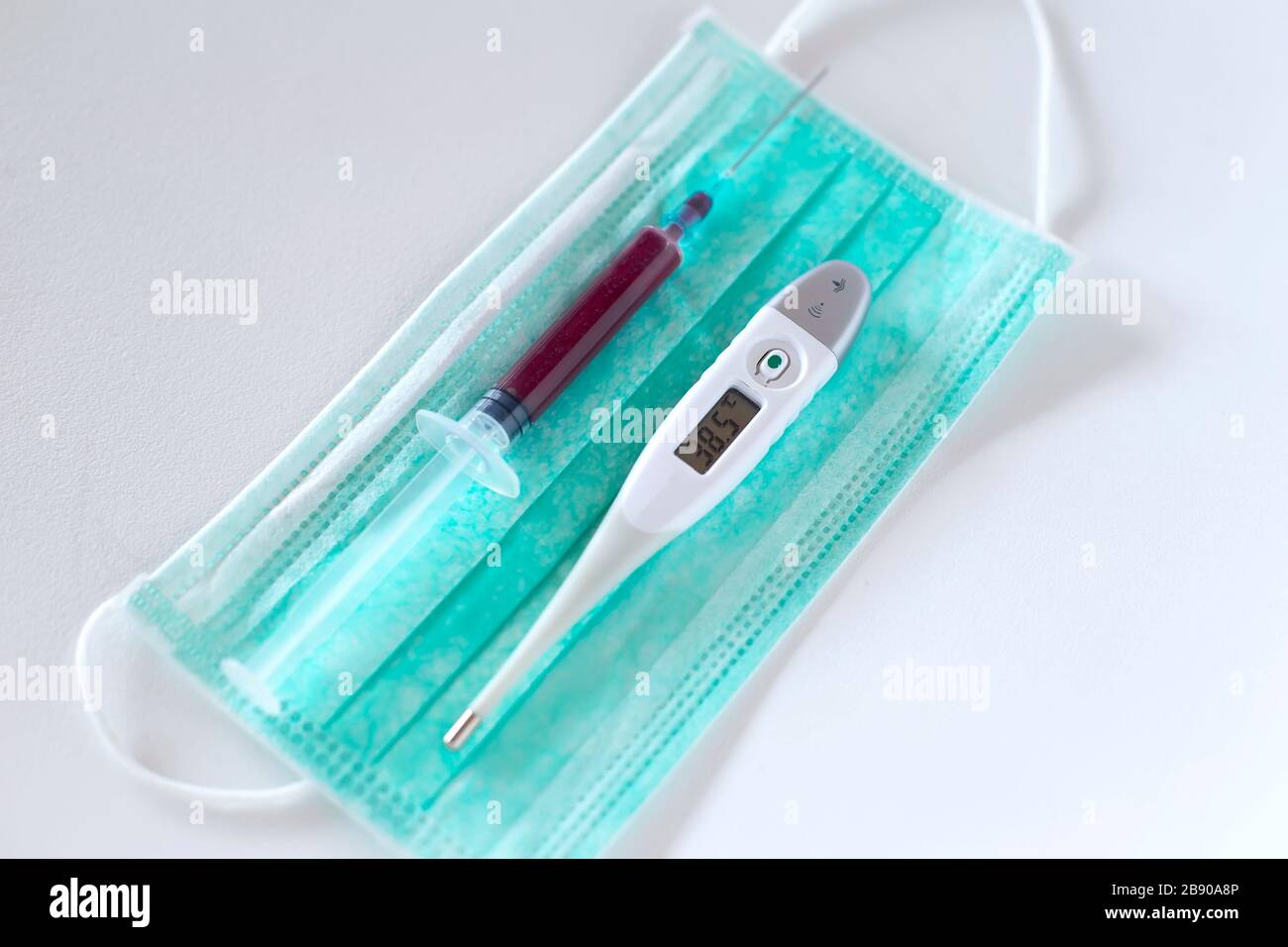 Surgical ear-loop mask, injection syringe and thermometer on the table ...
