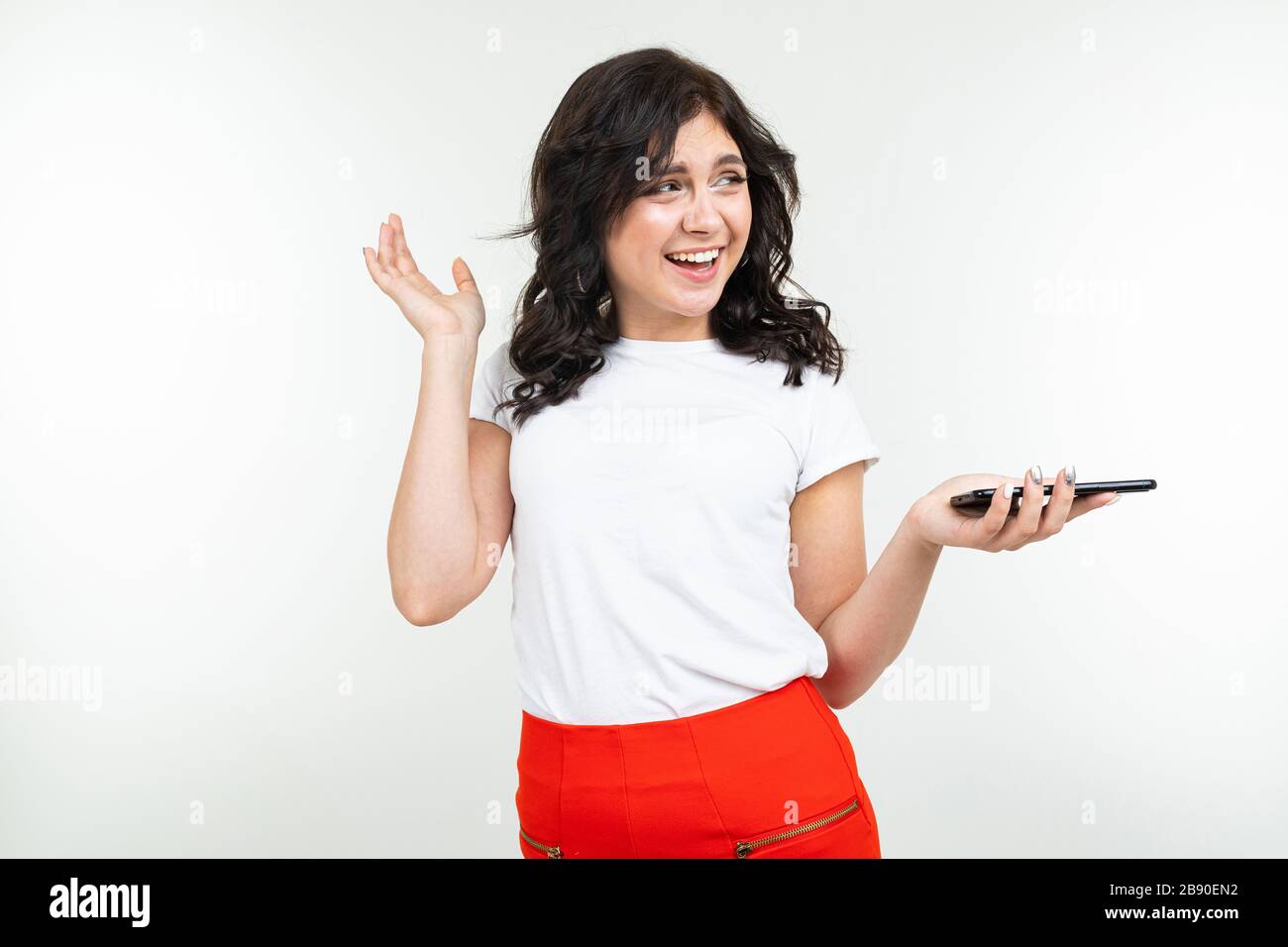 cute girl talking on the speakerphone of a phone on a white studio ...