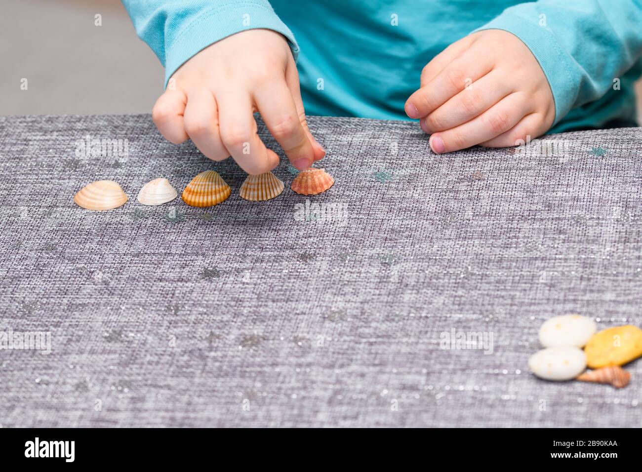 Five year old boy lining up seashells and pebbles on a table. Front ...