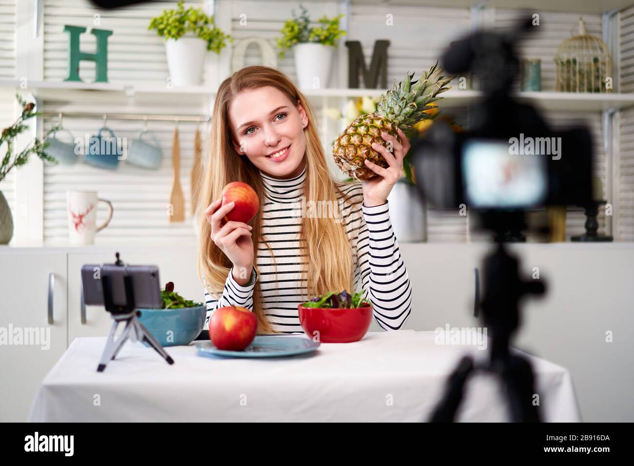 Food blogger cooking fresh vegan salad of fruits in kitchen studio ...