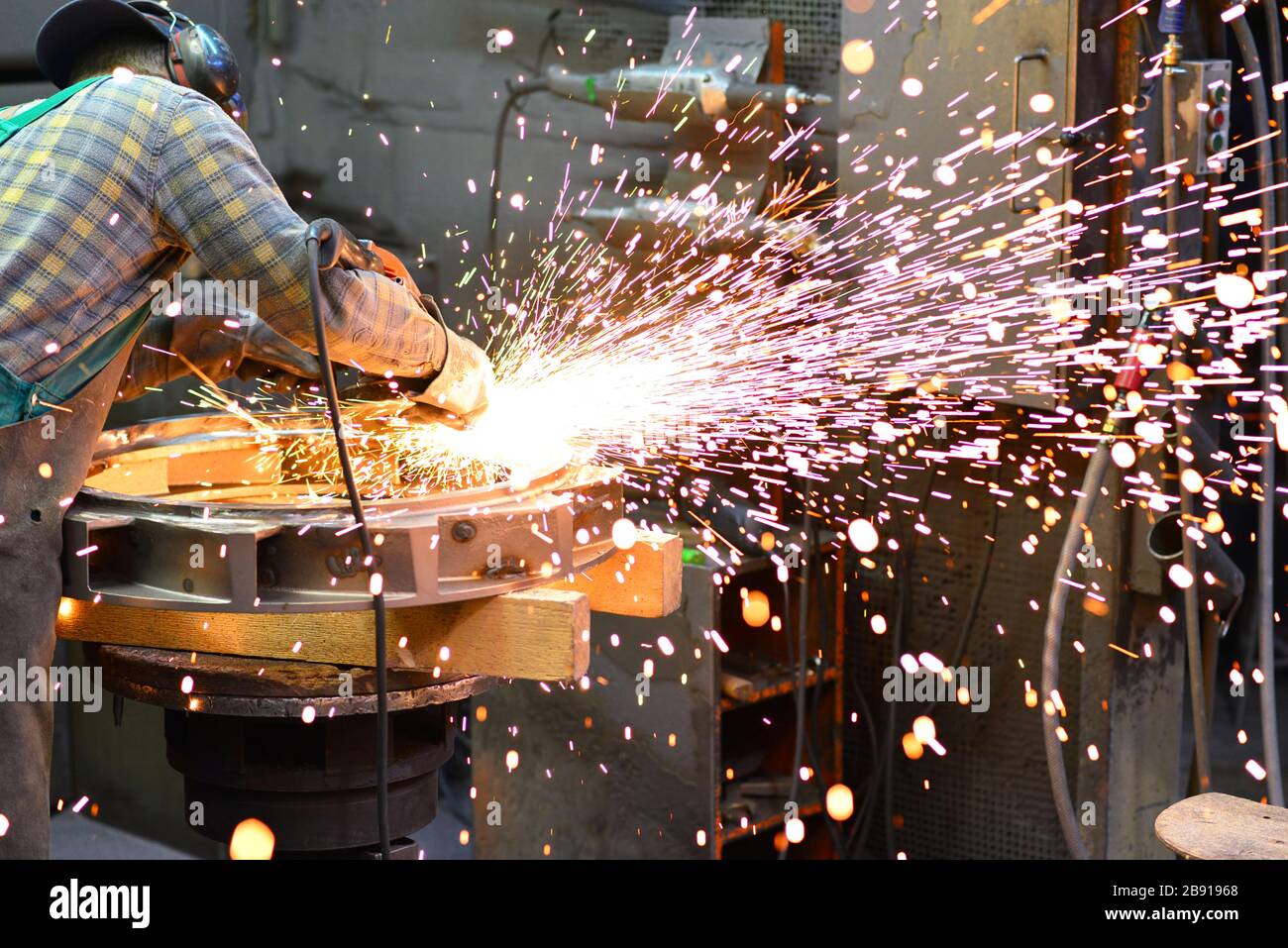 workers in safety clothing sanding a casting in an industrial company ...