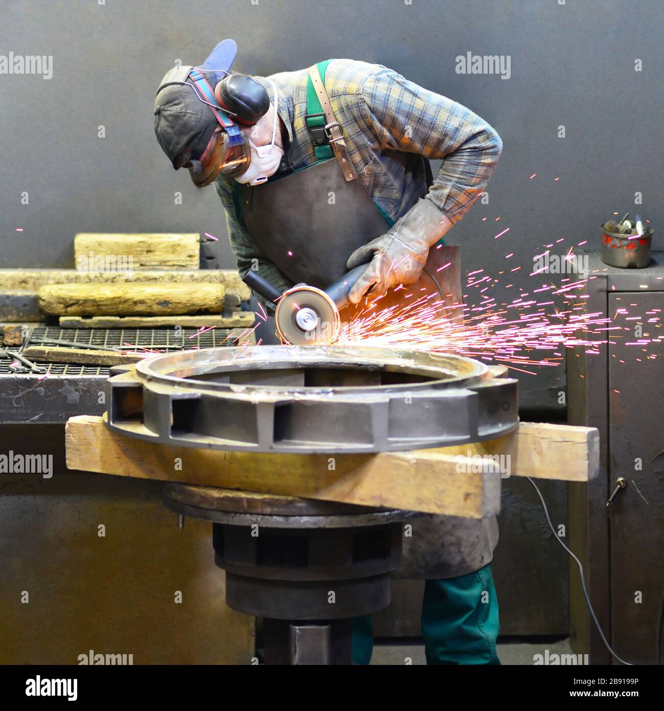 workers in safety clothing sanding a casting in an industrial company ...
