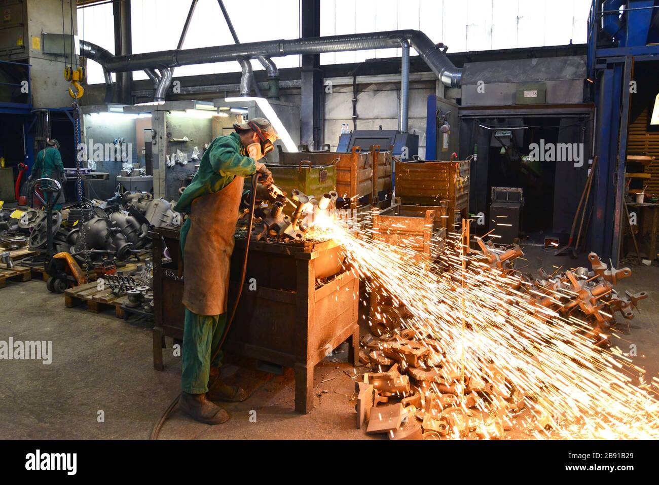 workers in safety clothing sanding a casting in an industrial company ...