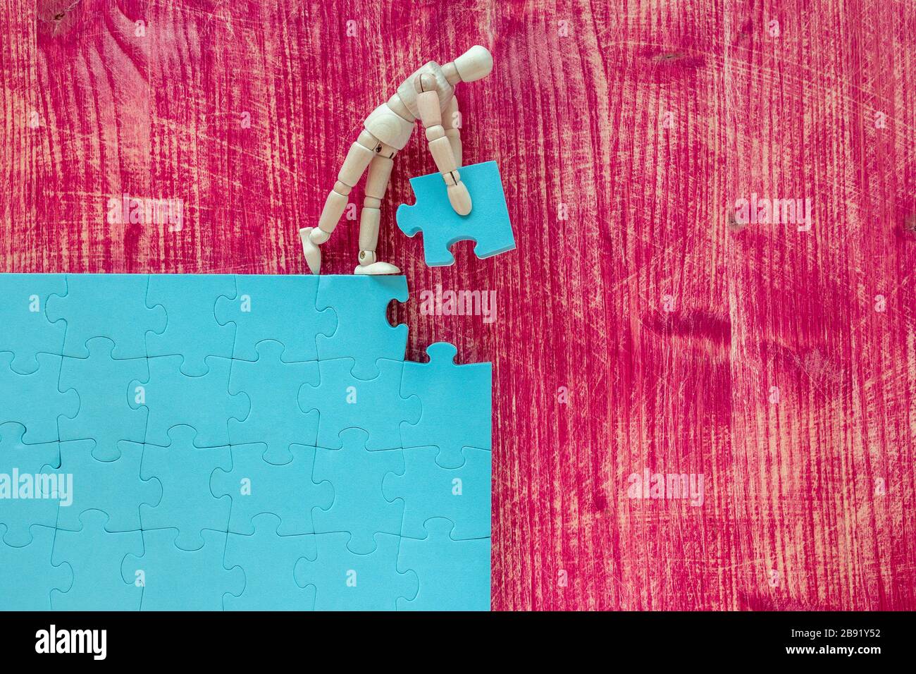 Wooden man assembling a jigsaw puzzle and adding the last missing piece ...