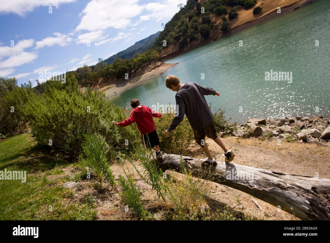 Two boys walking along a wooden log near a river Stock Photo - Alamy