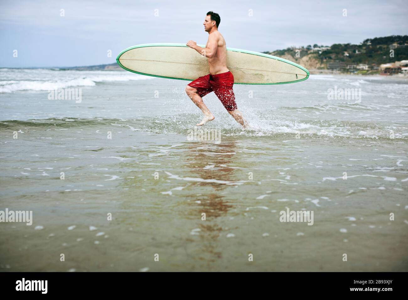 Man running into the ocean with his surfboard Stock Photo - Alamy