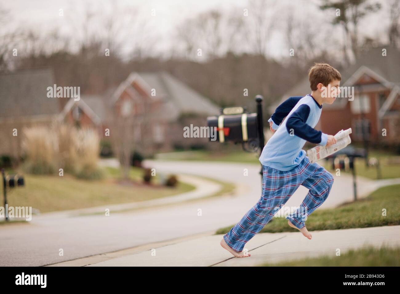 Boy running up driveway after collecting the newspaper from mailbox ...