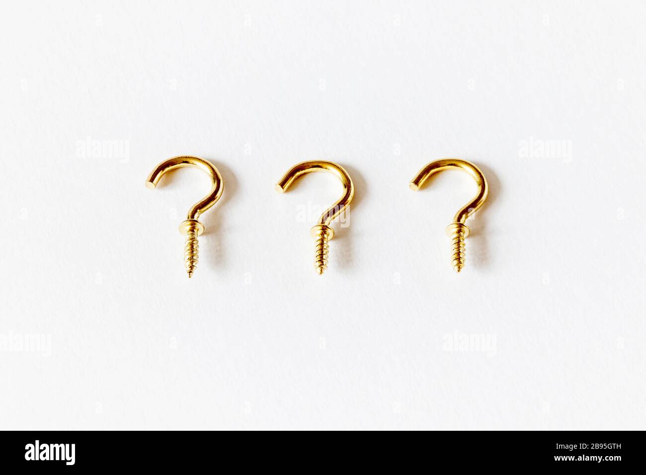 A horizontal line of three gold-coloured brass screw hooks on a white ...