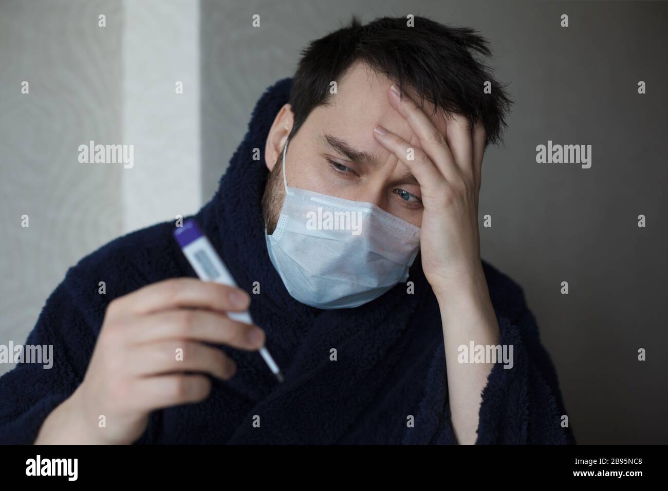 Worried man in medicine mask sit at home in dark gown and look at ...