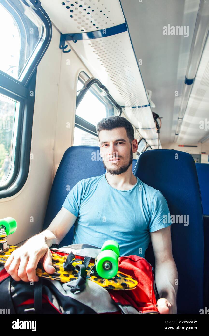 young pretty modern hipster guy traveller on train with skateboard ...