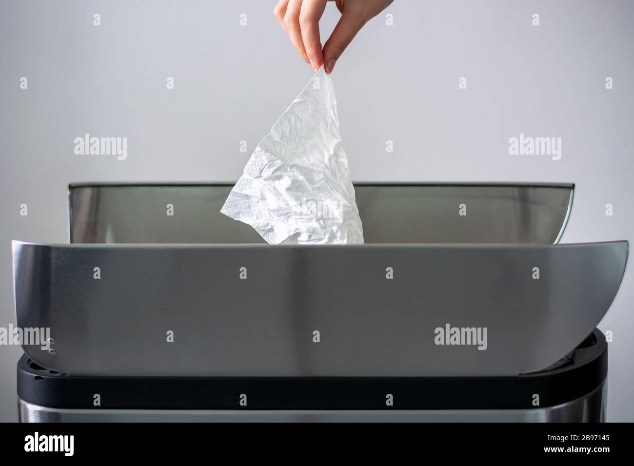 Women hand throwing a white used crumpled tissue paper into a trash bin ...