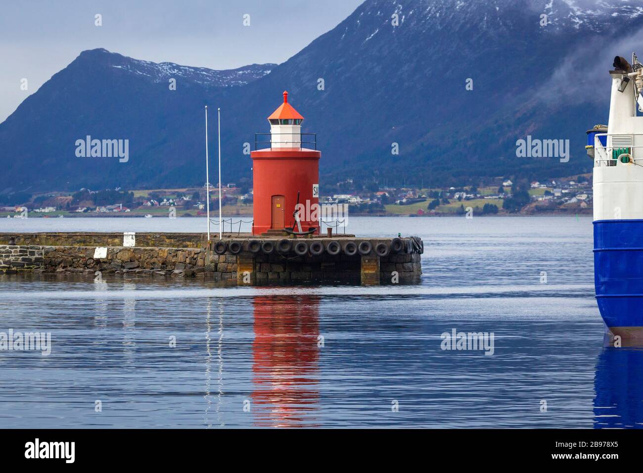 Red lighthouse and an old anchor at the port entrance of Alesund at the ...
