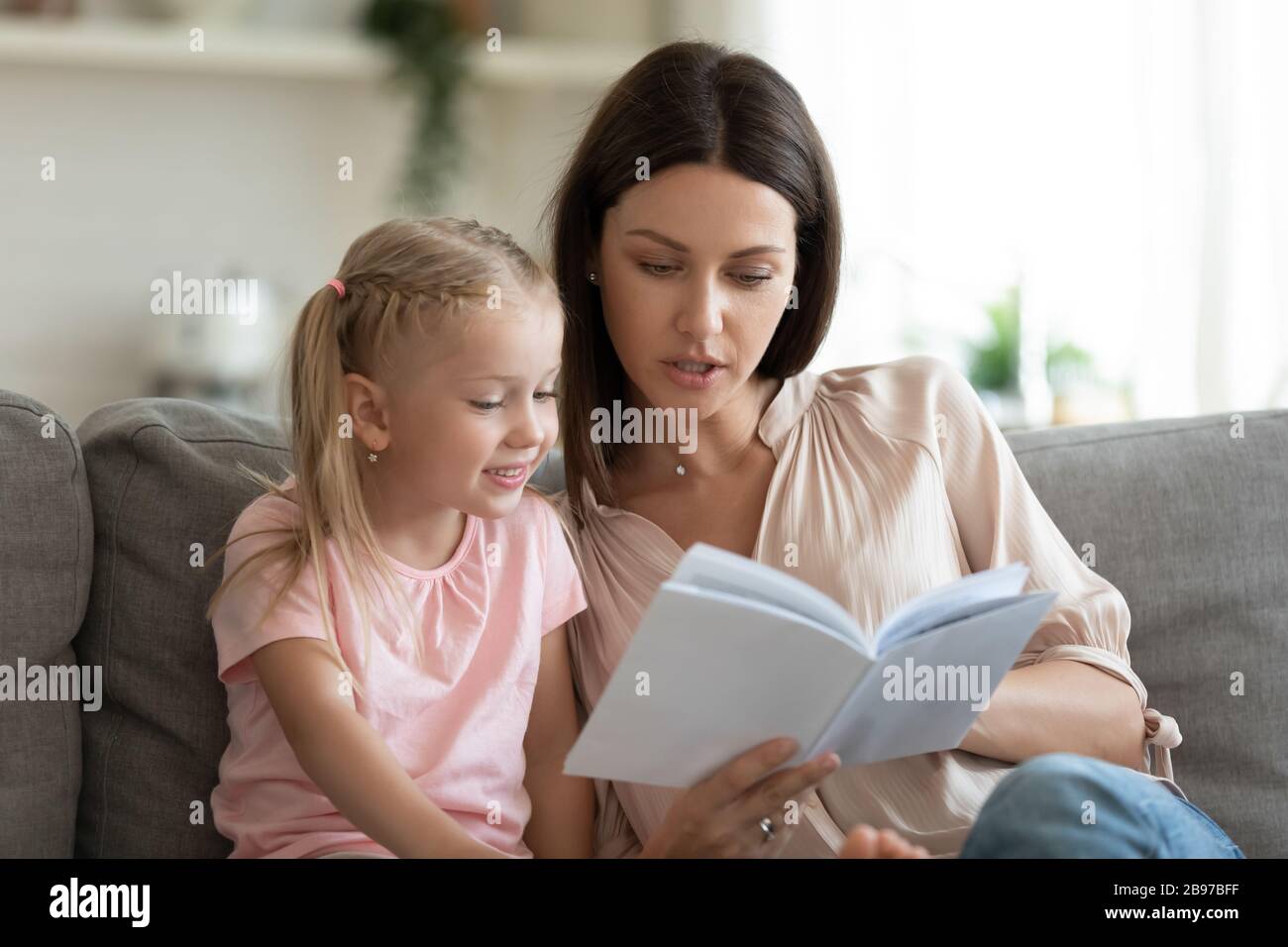 Little girl reading book with young mom Stock Photo - Alamy