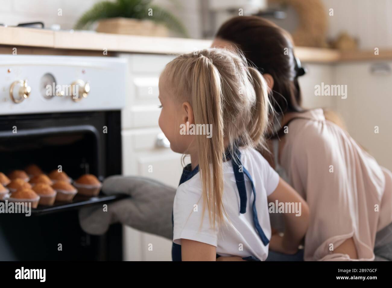 Excited little girl take ready muffins from oven Stock Photo - Alamy