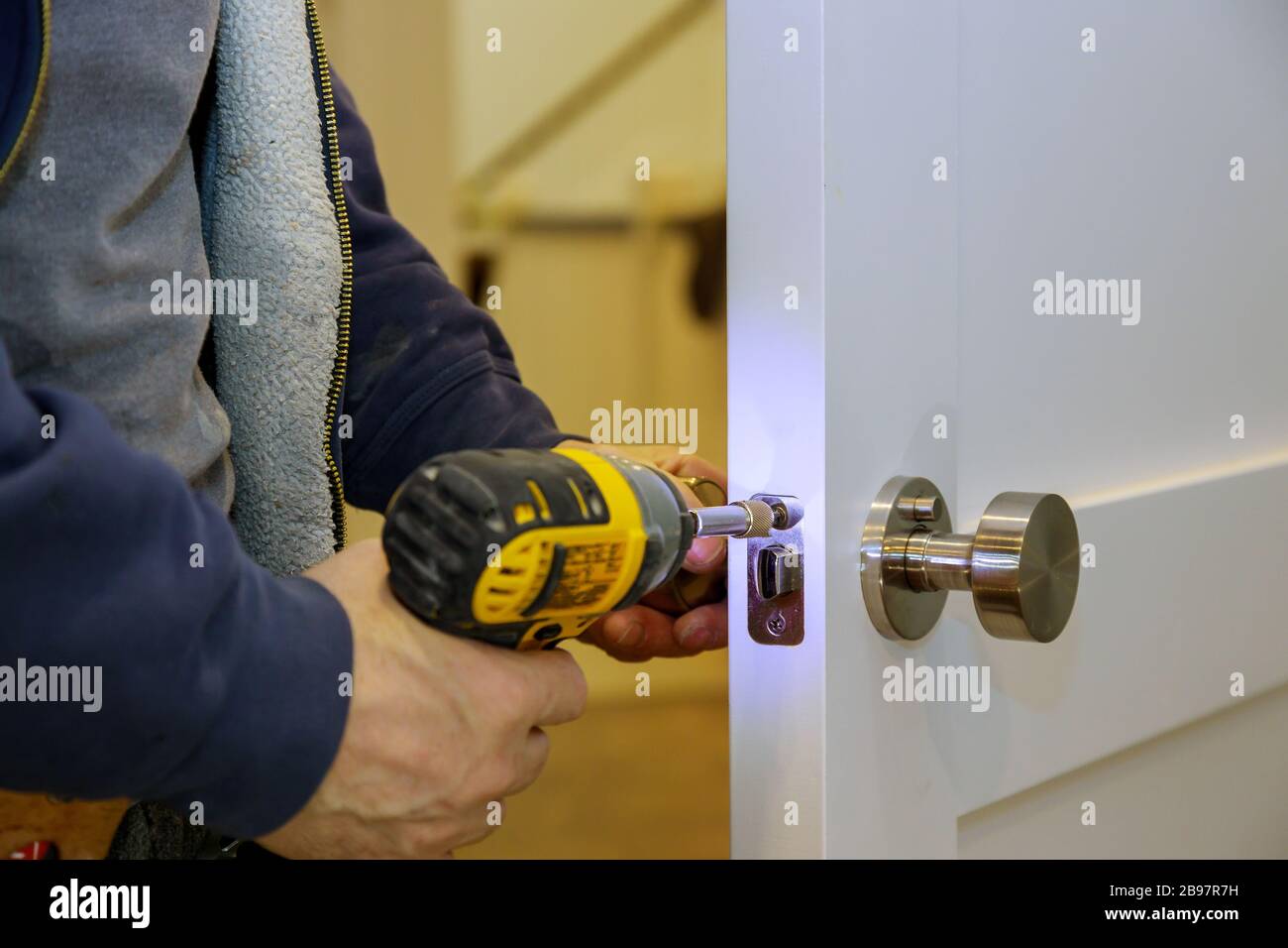 Handyman using a screwdriver drill to installing lock in door in a ...