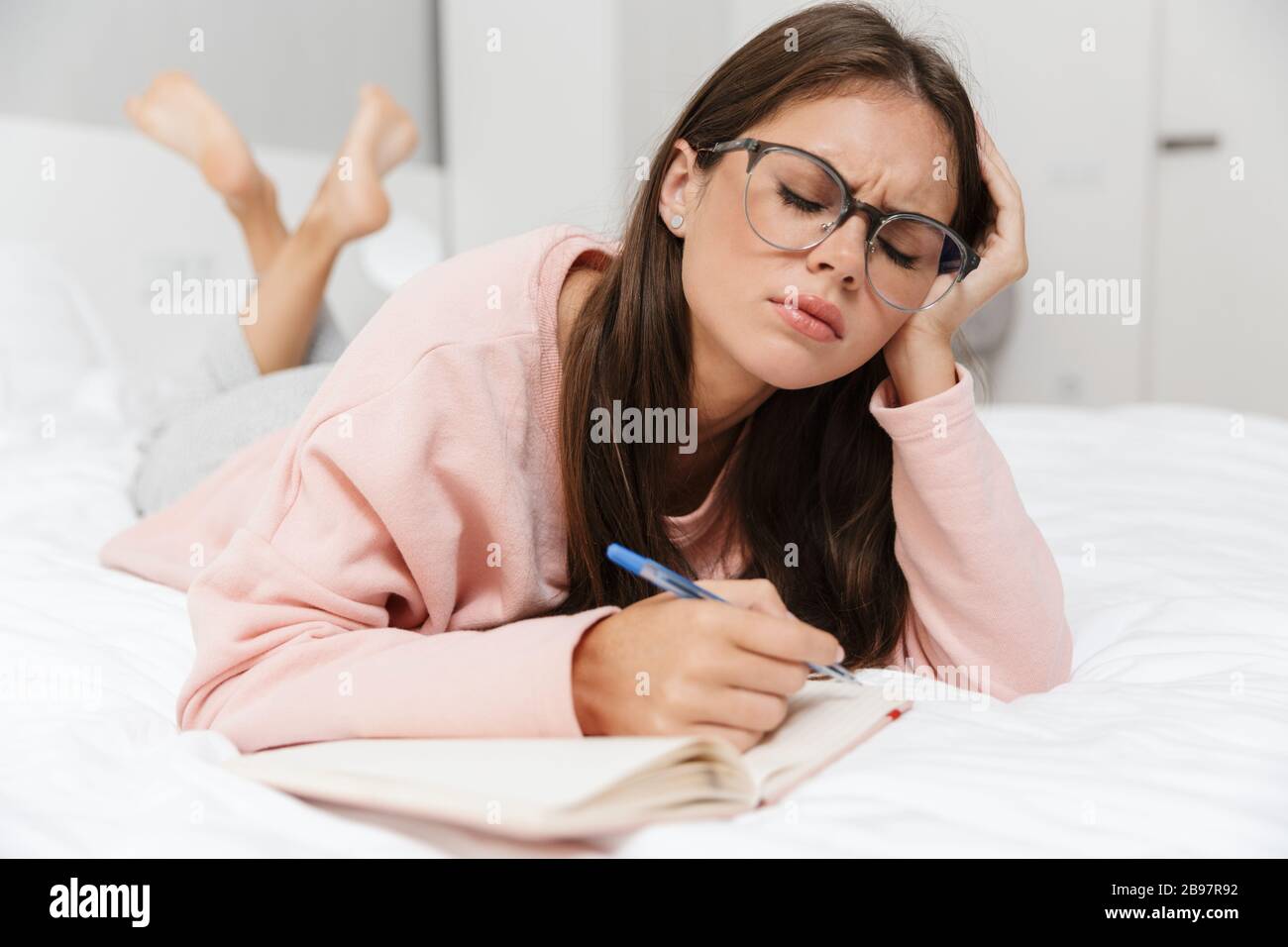 Upset lovely young girl wearing pajamas laying in bed at the bedroom ...