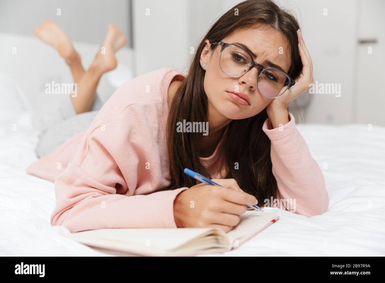 Upset lovely young girl wearing pajamas laying in bed at the bedroom ...