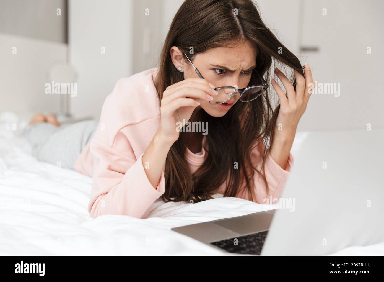 Confused lovely young girl wearing pajamas laying in bed at the bedroom ...