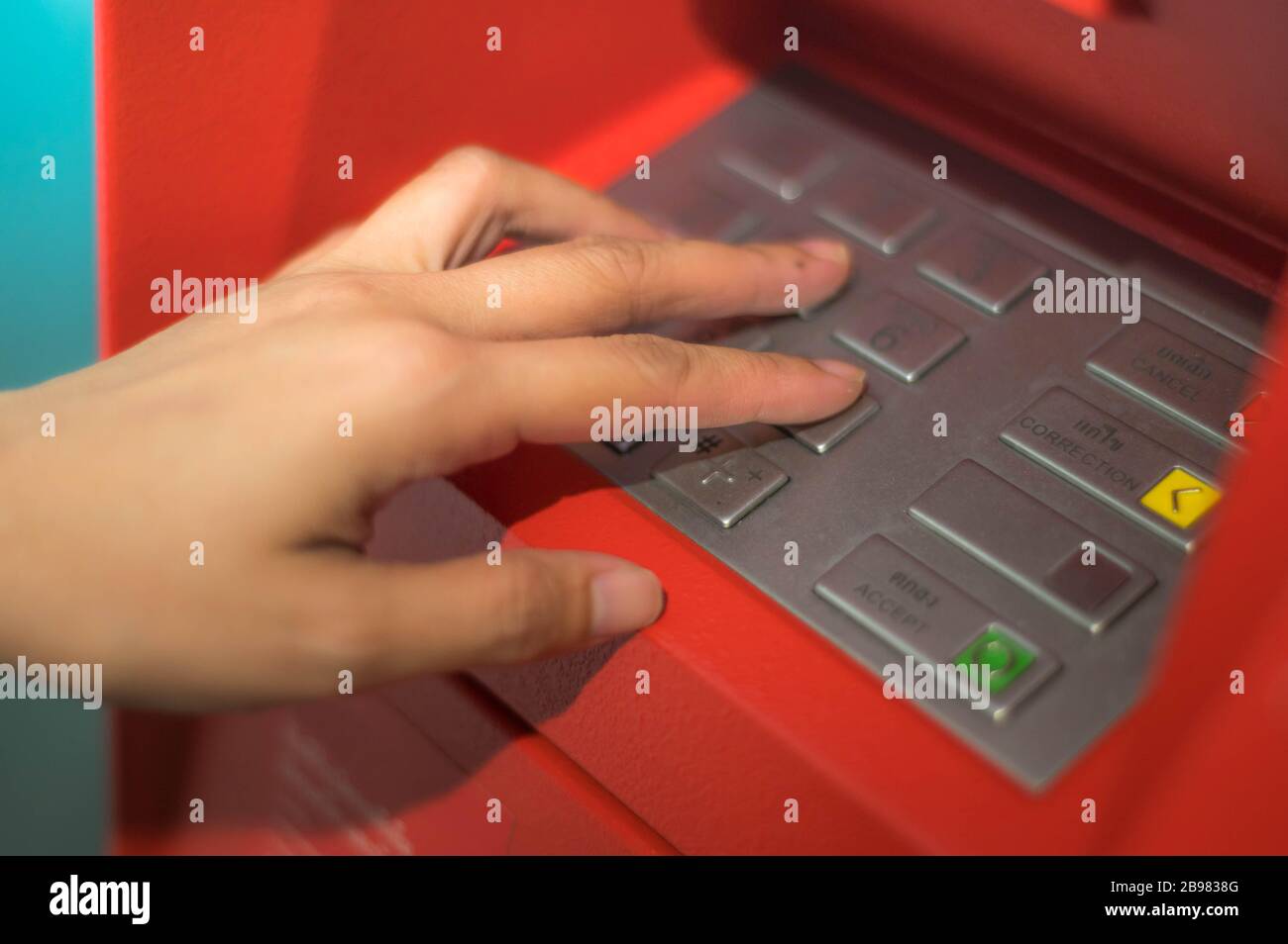 Woman hands to press the ATM key in the red cabinet. Finger pressing a pin code on a number pad ...