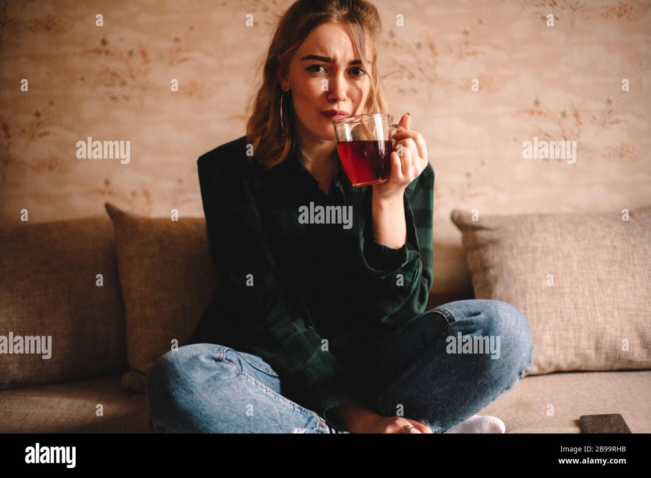 Young outraged woman drinking tea while sitting on sofa at home Stock ...