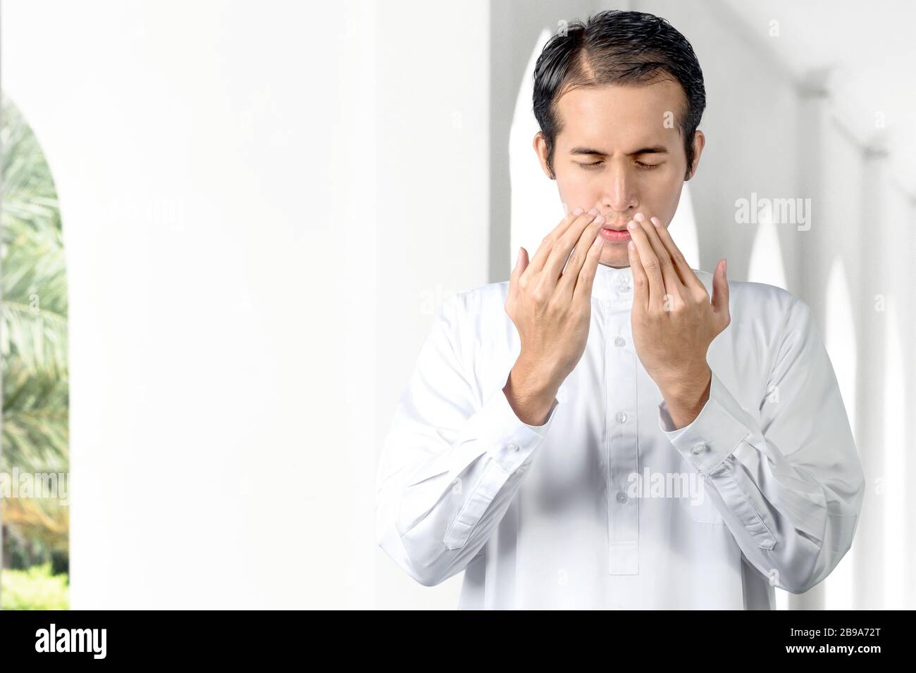 Asian Muslim man standing while raised hands and praying inside the ...