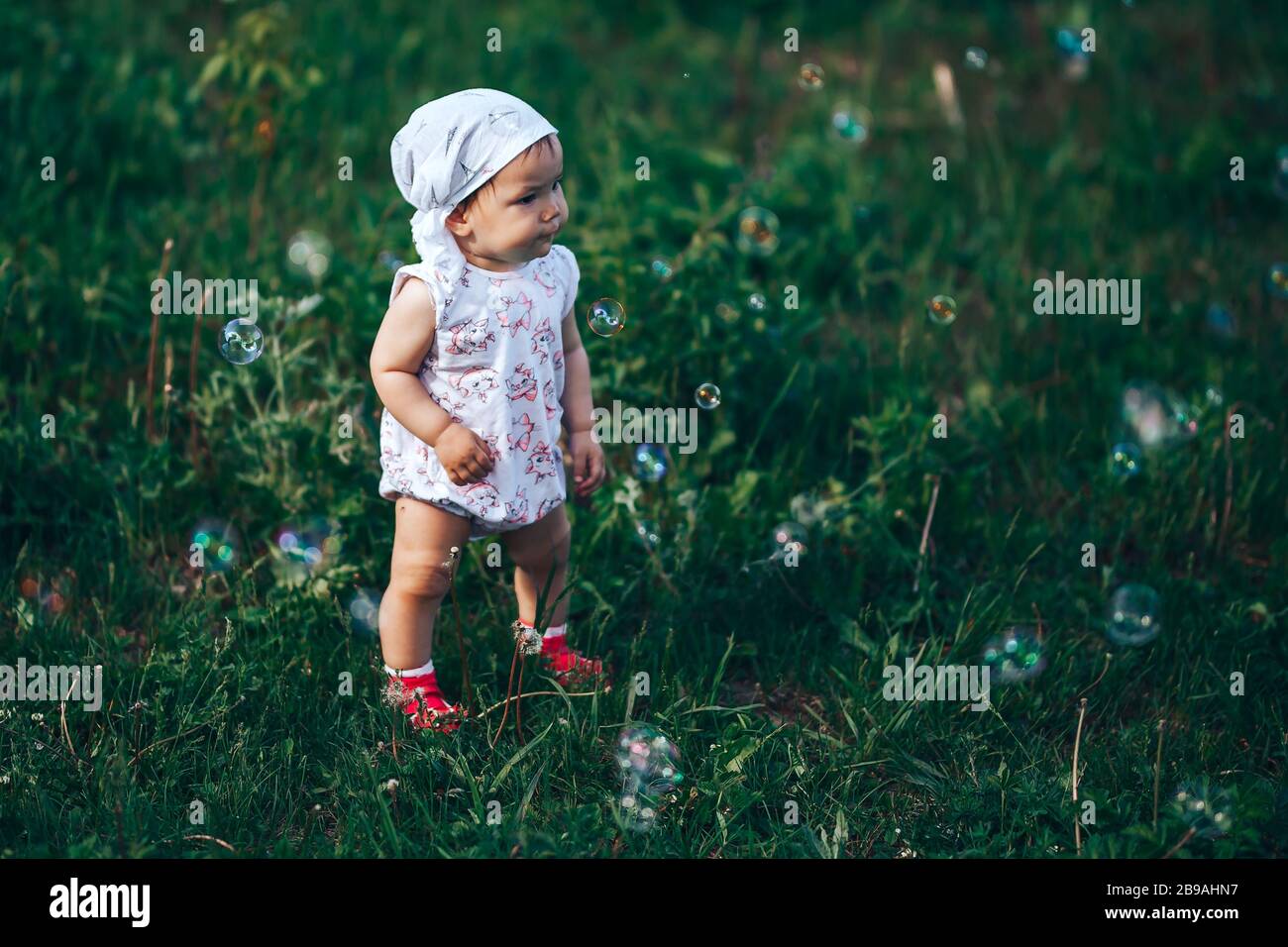 A little girl blowing soap bubbles, spring portrait beautiful one year ...