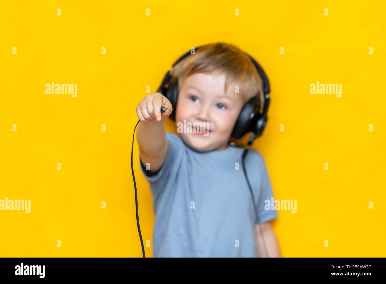 A smiling boy unplug his headphone and show plug to camera on isolated ...