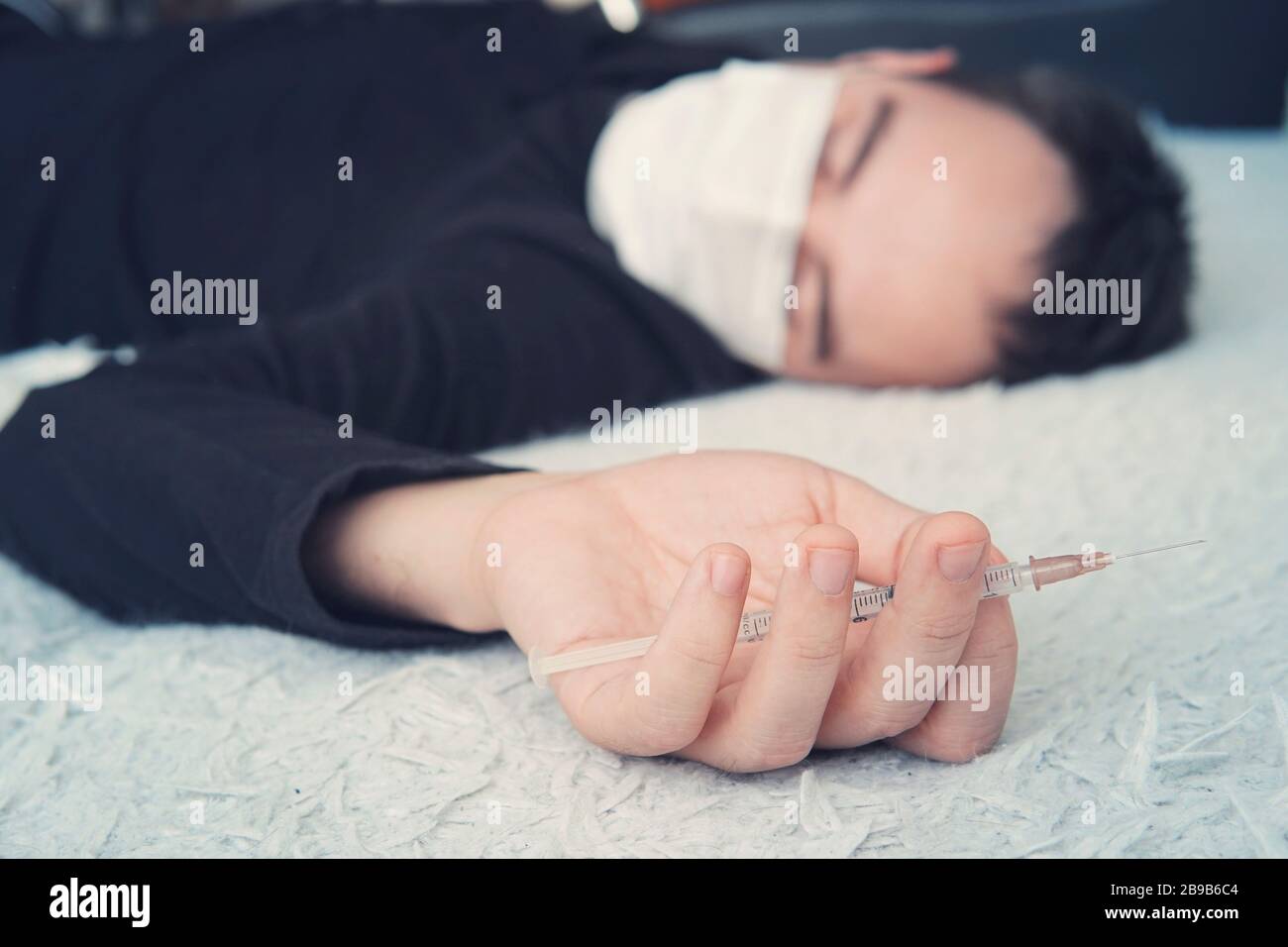 A young man is lying on the floor with a syringe in his hand. an ...