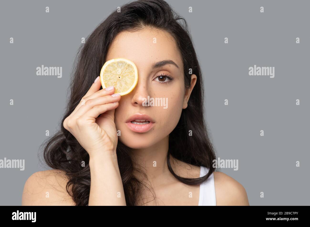 Beautiful dark-haired girl closing one eye with an orange half Stock ...