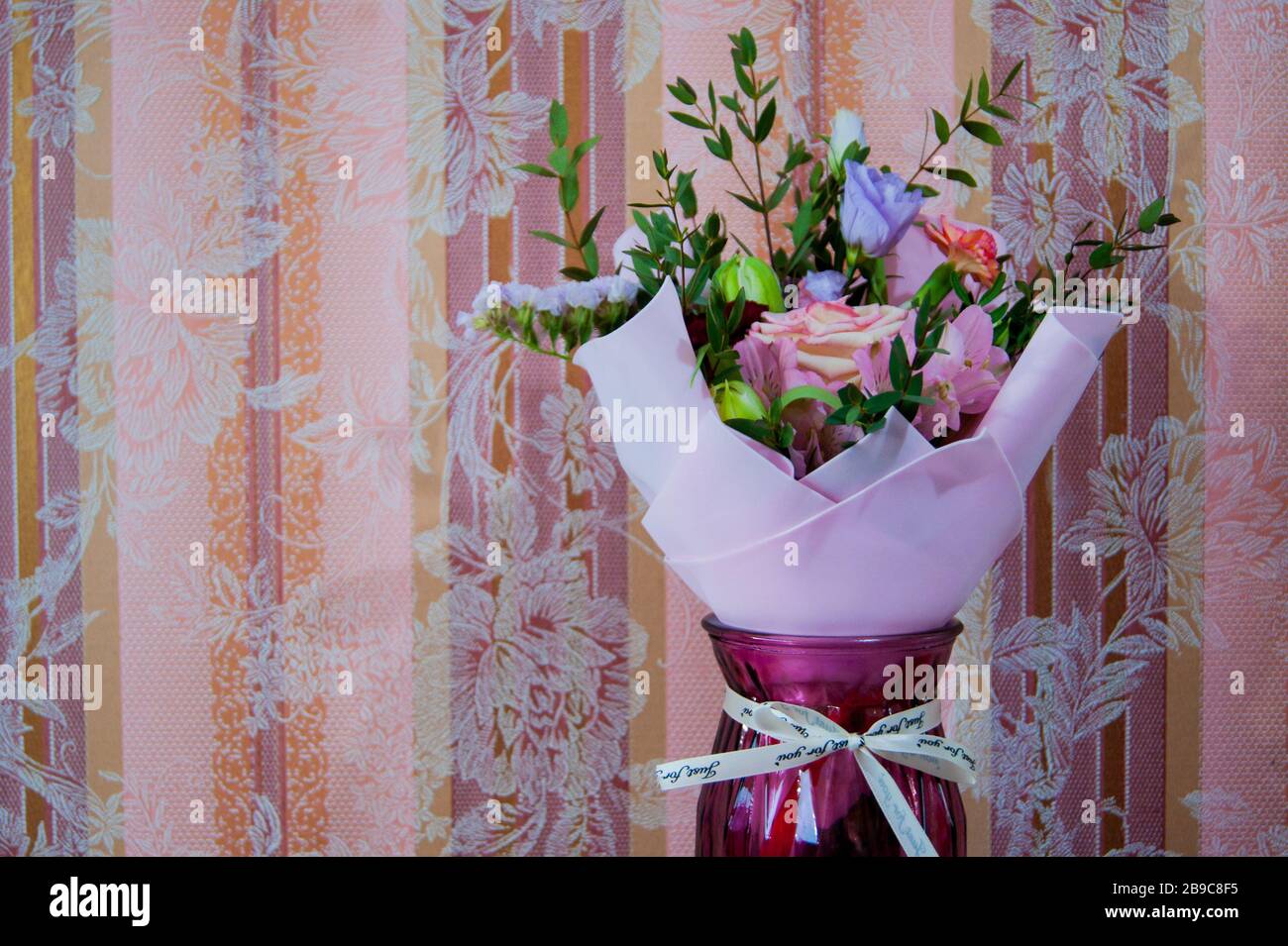 A delicate bouquet of different flowers in a light pink wrapper stands ...