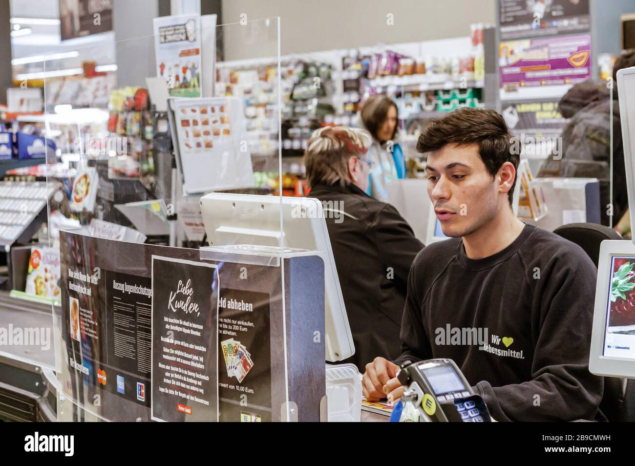 Berlin, Germany. 23rd Mar, 2020. A cashier works behind a shield at a ...