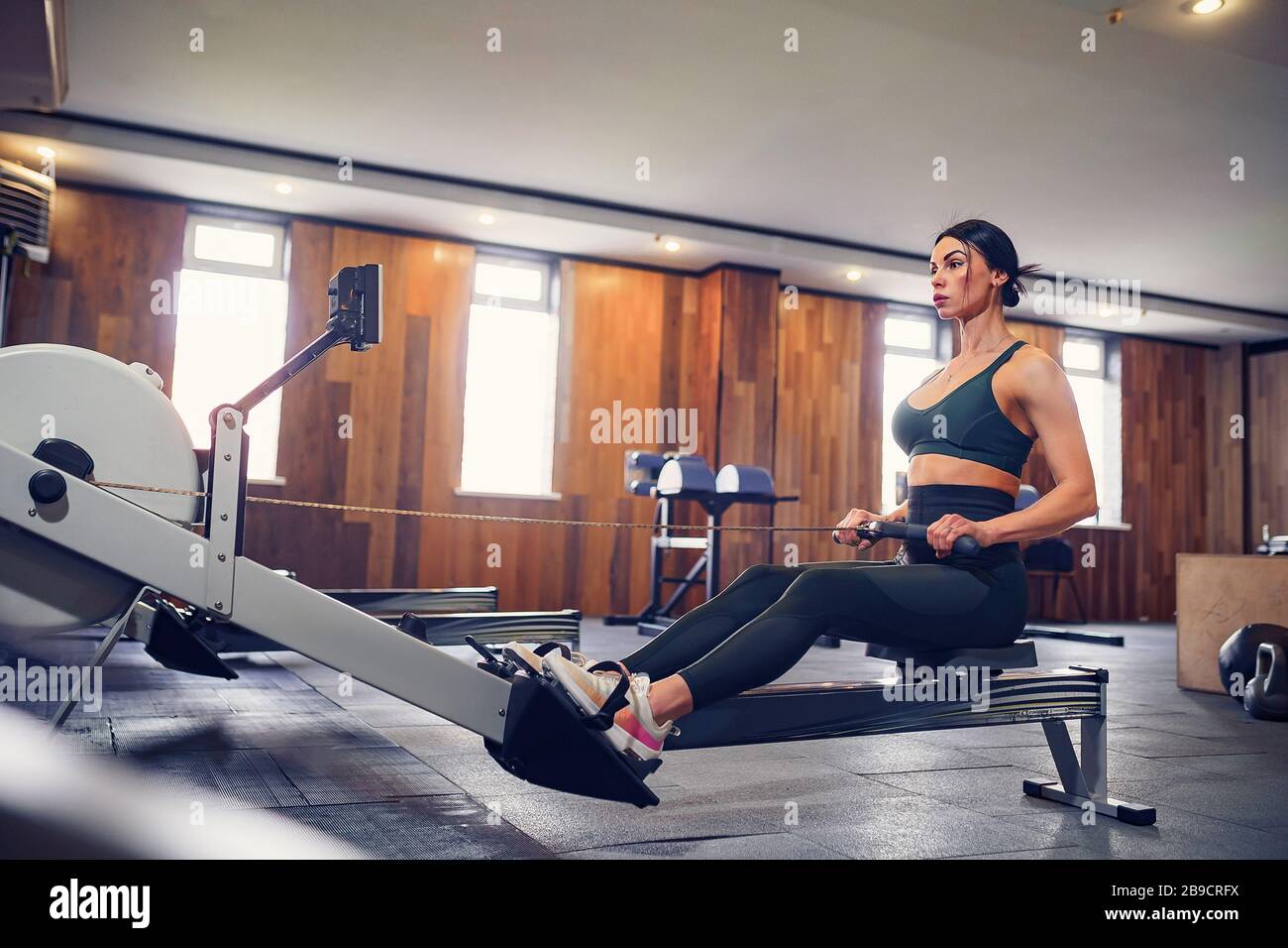 Determined young woman working out on row machine in fitness studio ...