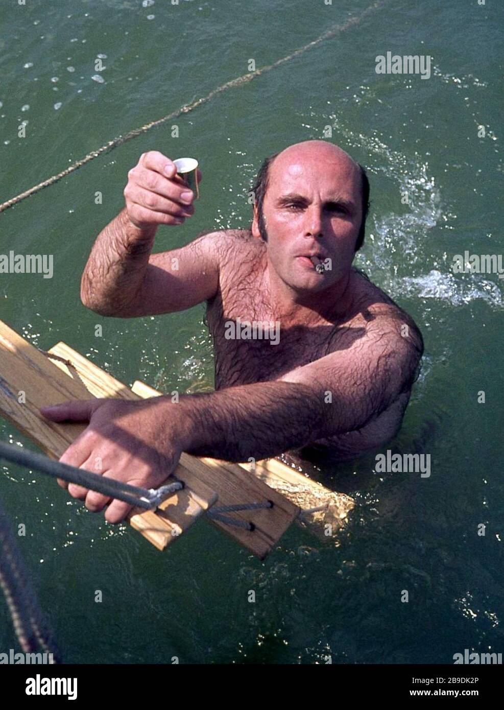 A man holds on to a rope ladder hanging from a boat and cheers to the ...