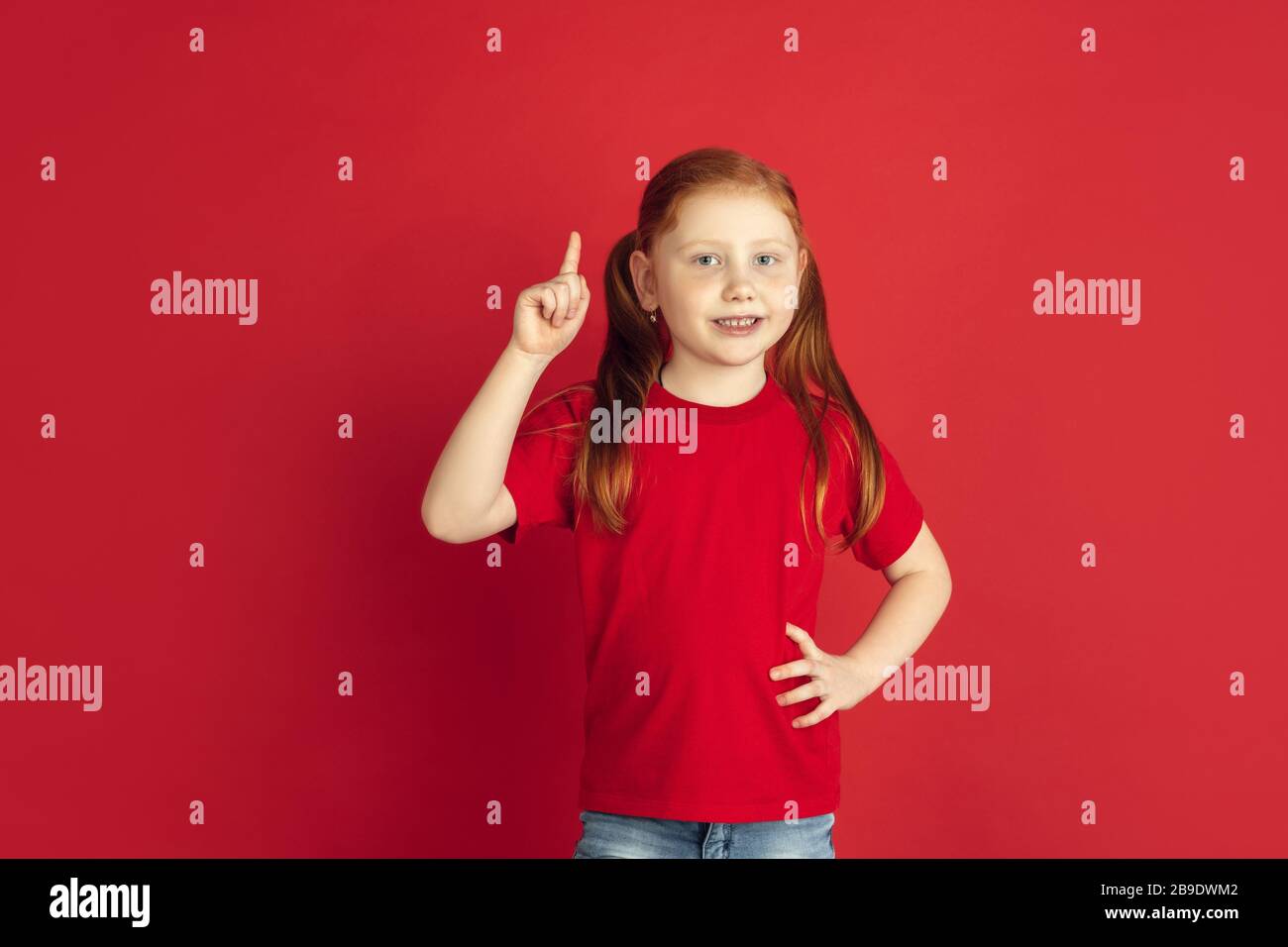 Pointing up. Caucasian little girl portrait isolated on red studio ...