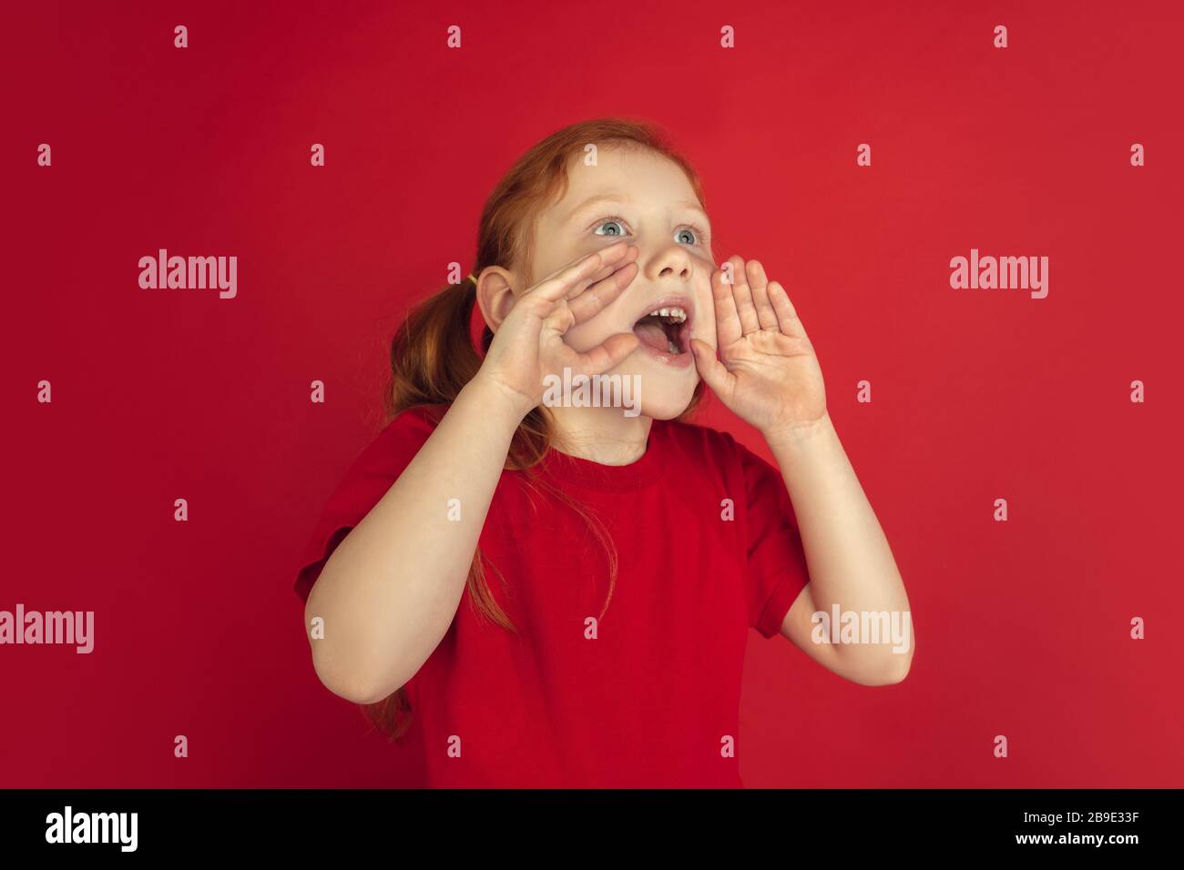 Calling, shouting. Caucasian little girl portrait isolated on red ...
