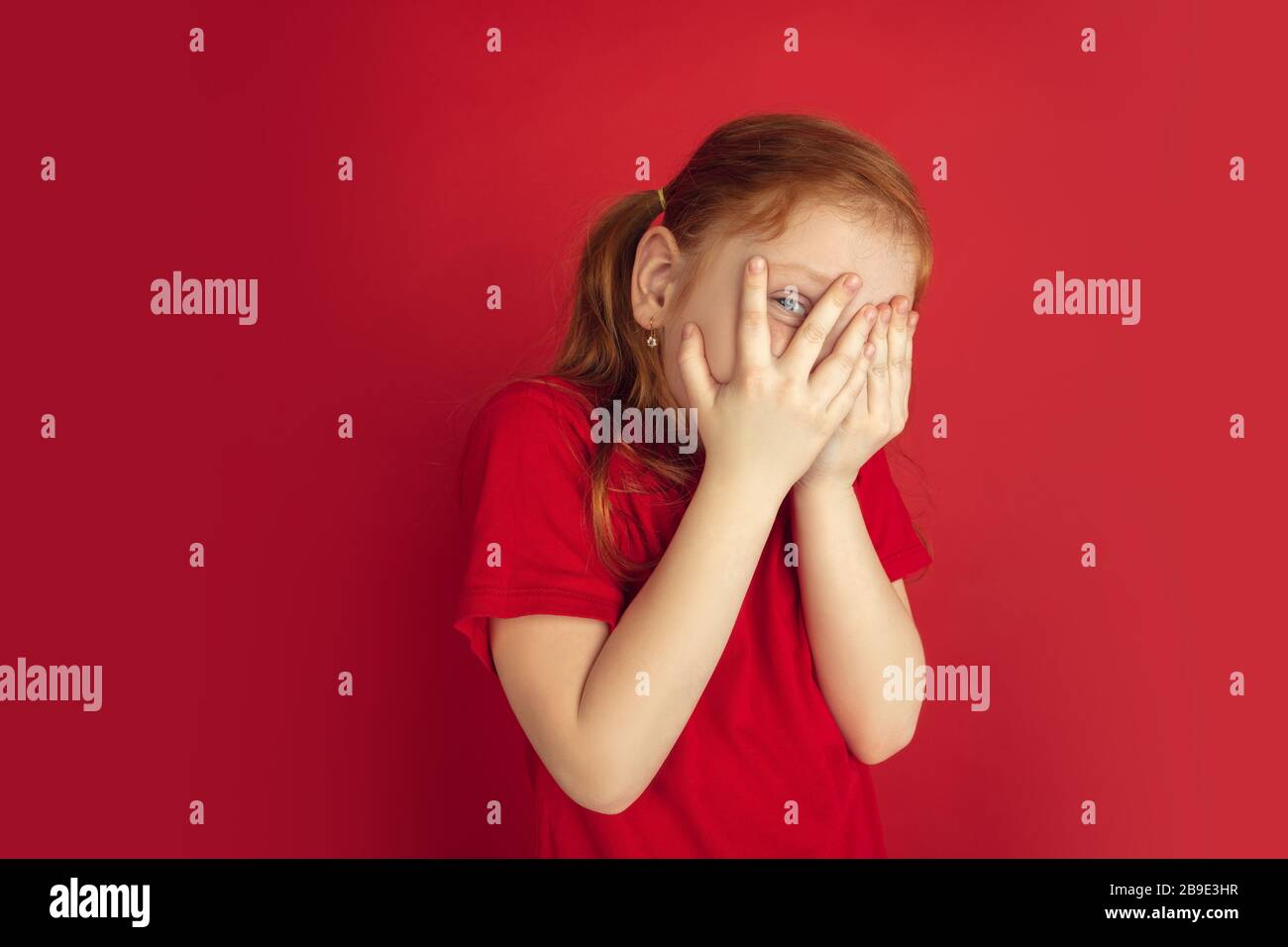 Scared hiding face. Caucasian little girl portrait isolated on red ...